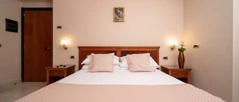 Quarto de hotel com uma cama grande, duas mesas de cabeceira, uma cabeceira de madeira e duas luminárias fixadas na parede.