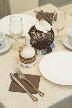 Mesa posta com pratos brancos, talheres e um vaso de vidro decorativo com uma orquídea.