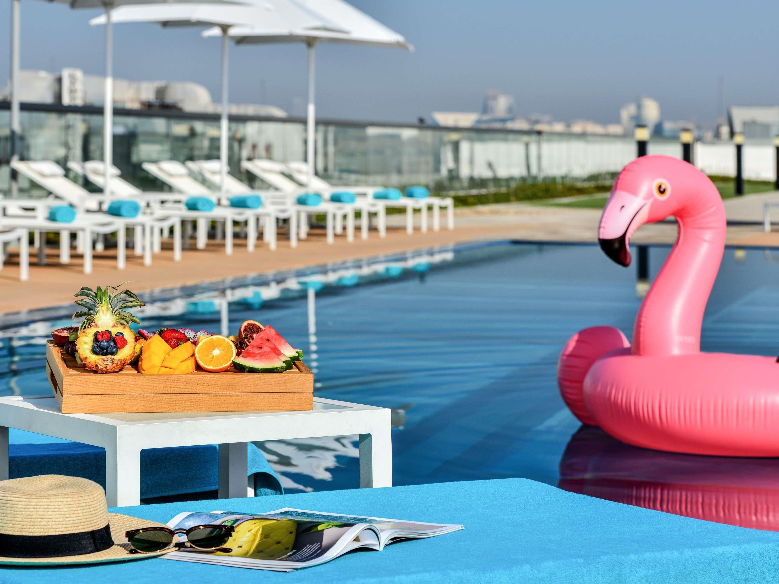 Uma área junto à piscina com uma cesta de frutas, um boi flamingo flutuante, cadeiras de descanso e guarda-sóis.