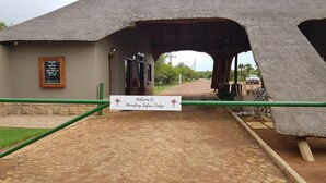 Placa de boas-vindas aos visitantes do Monateng Safari Lodge, com um telhado de palha rústico e entrada pavimentada.