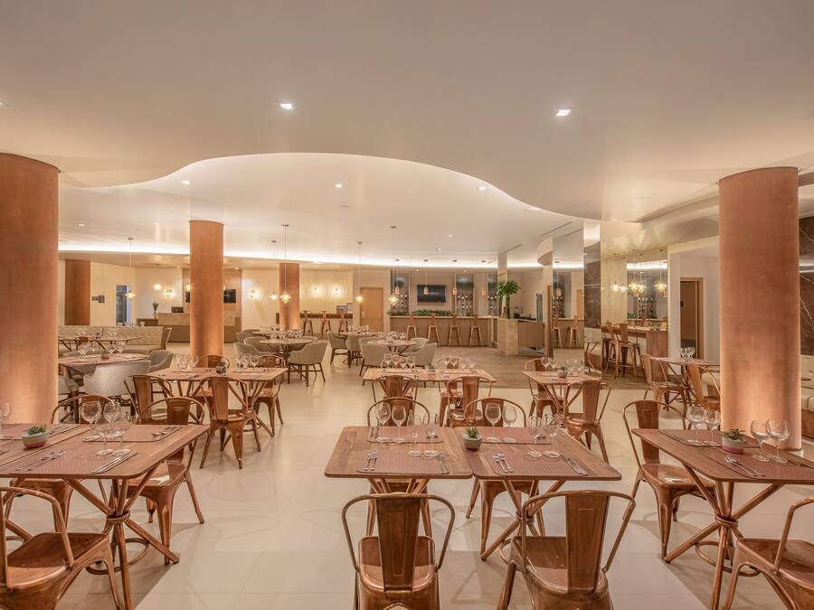 Um restaurante espaçoso com pé-direito alto, iluminação moderna e diversos tipos de assentos.