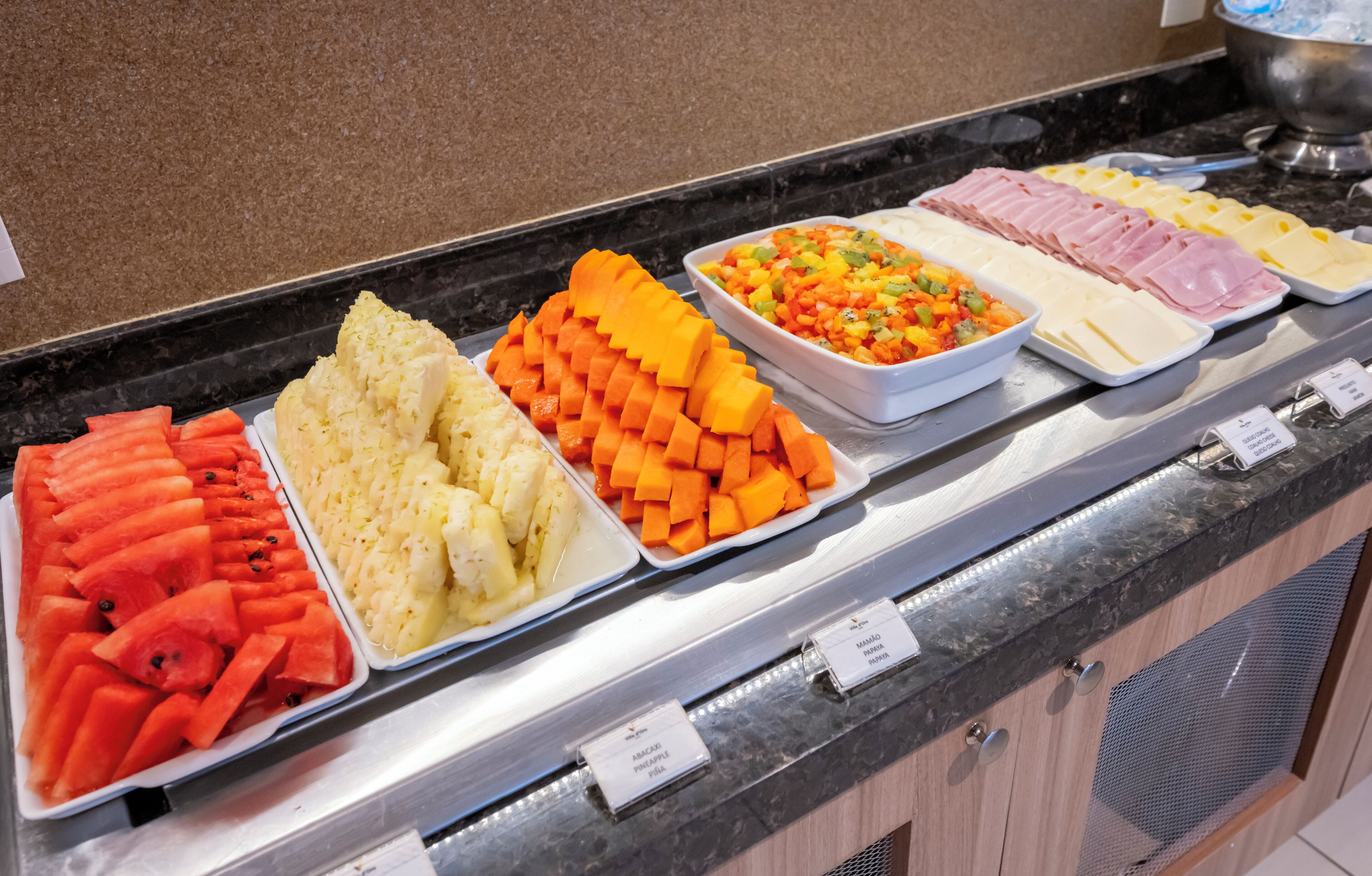 Buffet com diversos alimentos, incluindo melancia, abacaxi, queijo e presunto.