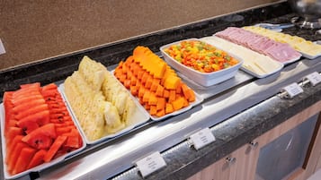 Buffet com diversos alimentos, incluindo melancia, abacaxi, queijo e presunto.