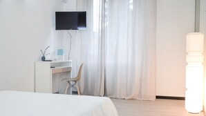 Quarto de hotel com cama, escrivaninha, cadeira, televisão e abajur.