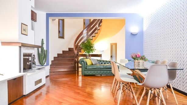 Um espaço de estar moderno com escada de madeira, um sofá verde, uma mesa de jantar com cadeiras e um cacto no balcão.