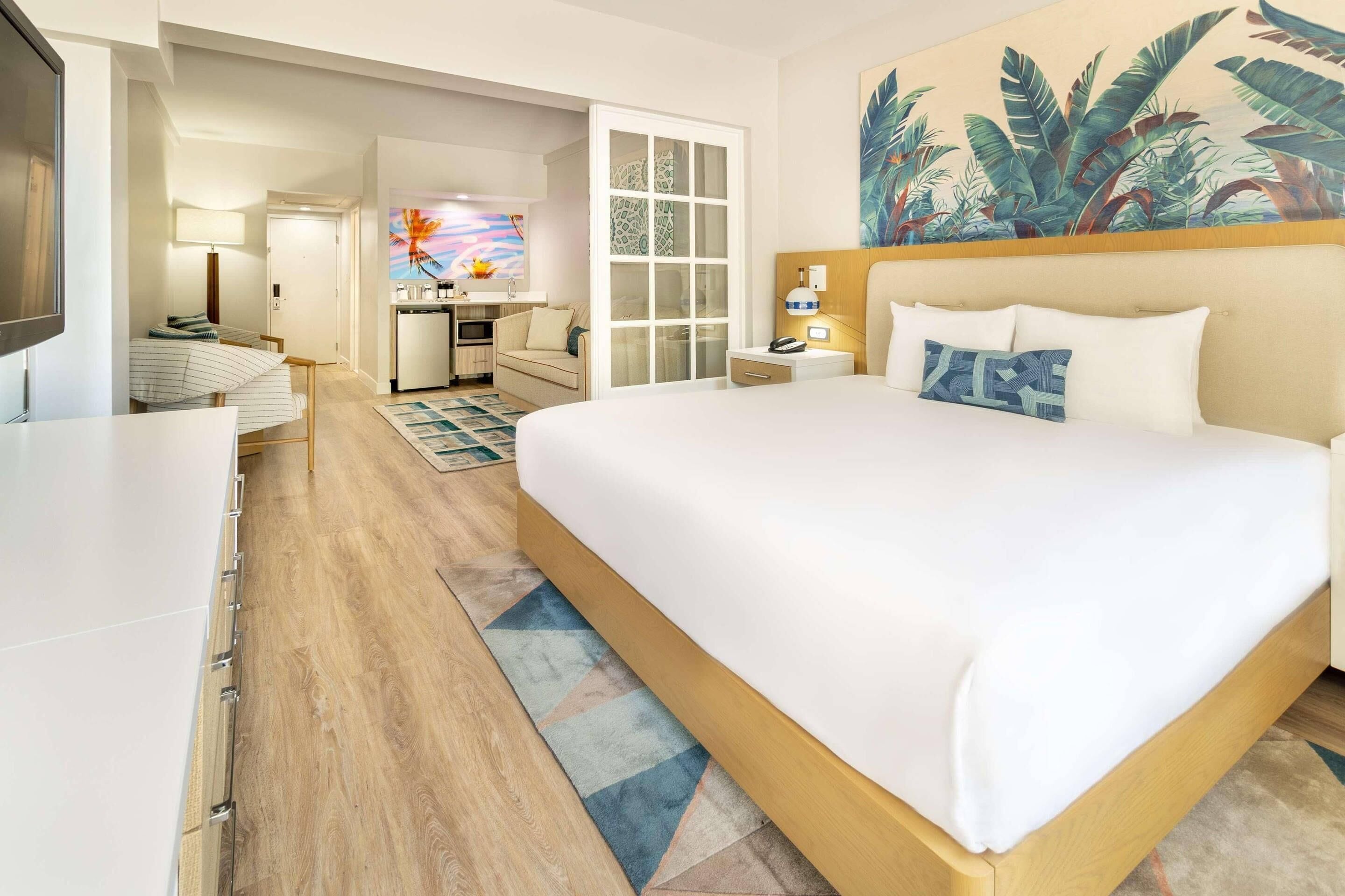 Quarto de hotel com uma cama grande, uma escrivaninha, uma cadeira, uma kitchenette pequena e um banheiro.