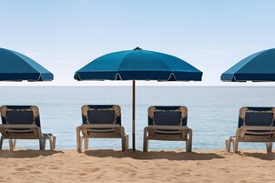 Na praia, espreguiçadeiras, guarda-sóis, toalhas de praia 
