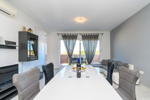 Uma sala de estar moderna com uma mesa de jantar, sofás cinzas e uma televisão de tela plana.
