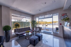 Um lobby moderno com sofá, cadeiras, mesa de centro e uma grande planta em vaso.