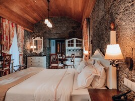Um quarto aconchegante com uma cama grande, teto de madeira, paredes de pedra e uma cozinha rústica ao fundo.