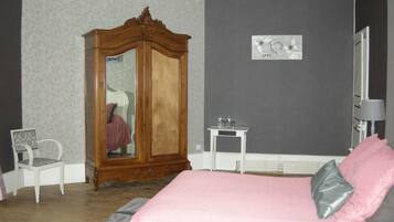 Um quarto com um guarda-roupa de madeira grande, uma cama com roupa de cama rosa, uma mesinha de cabeceira pequena e um espelho.