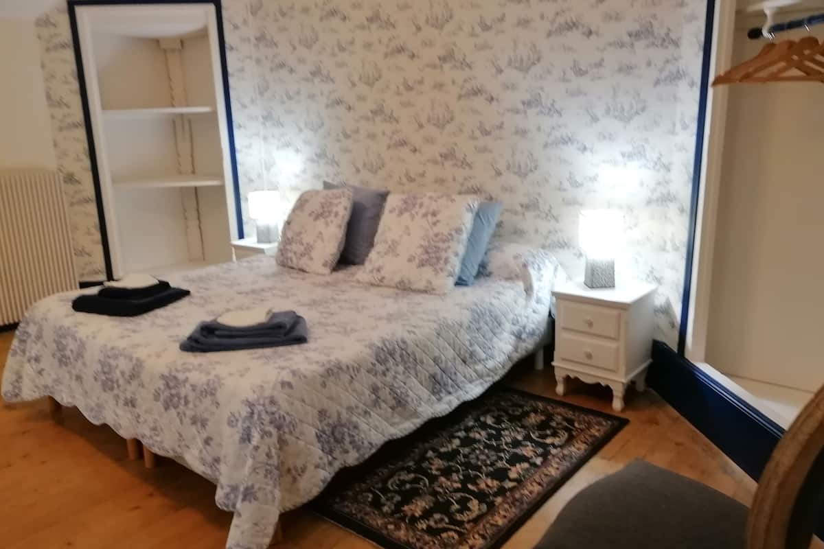 Quarto com cama, mesa de cabeceira, cadeira e tapete estampado.
