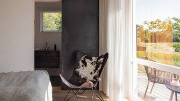 Um quarto acolhedor com uma janela ampla, uma cadeira, uma mesinha e vista para um jardim.