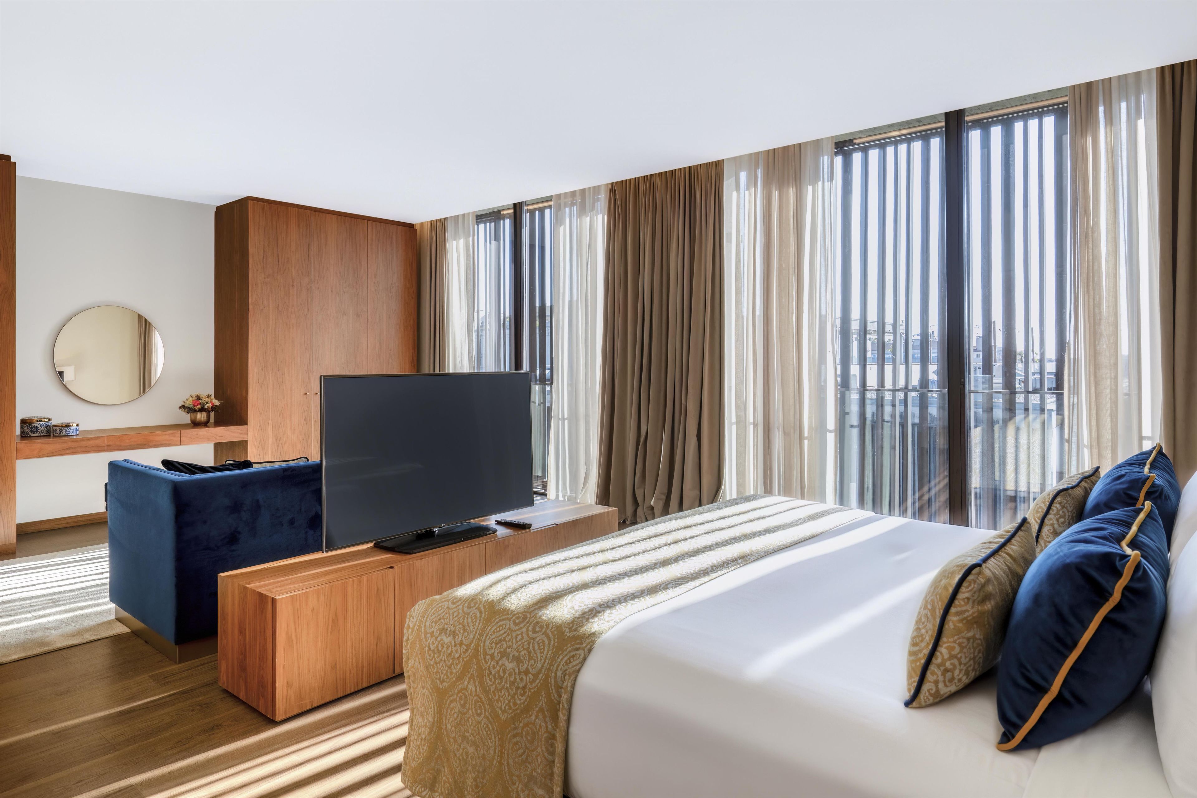 Quarto de hotel moderno com uma cama grande, televisão de tela plana, sofá e um armário de madeira.
