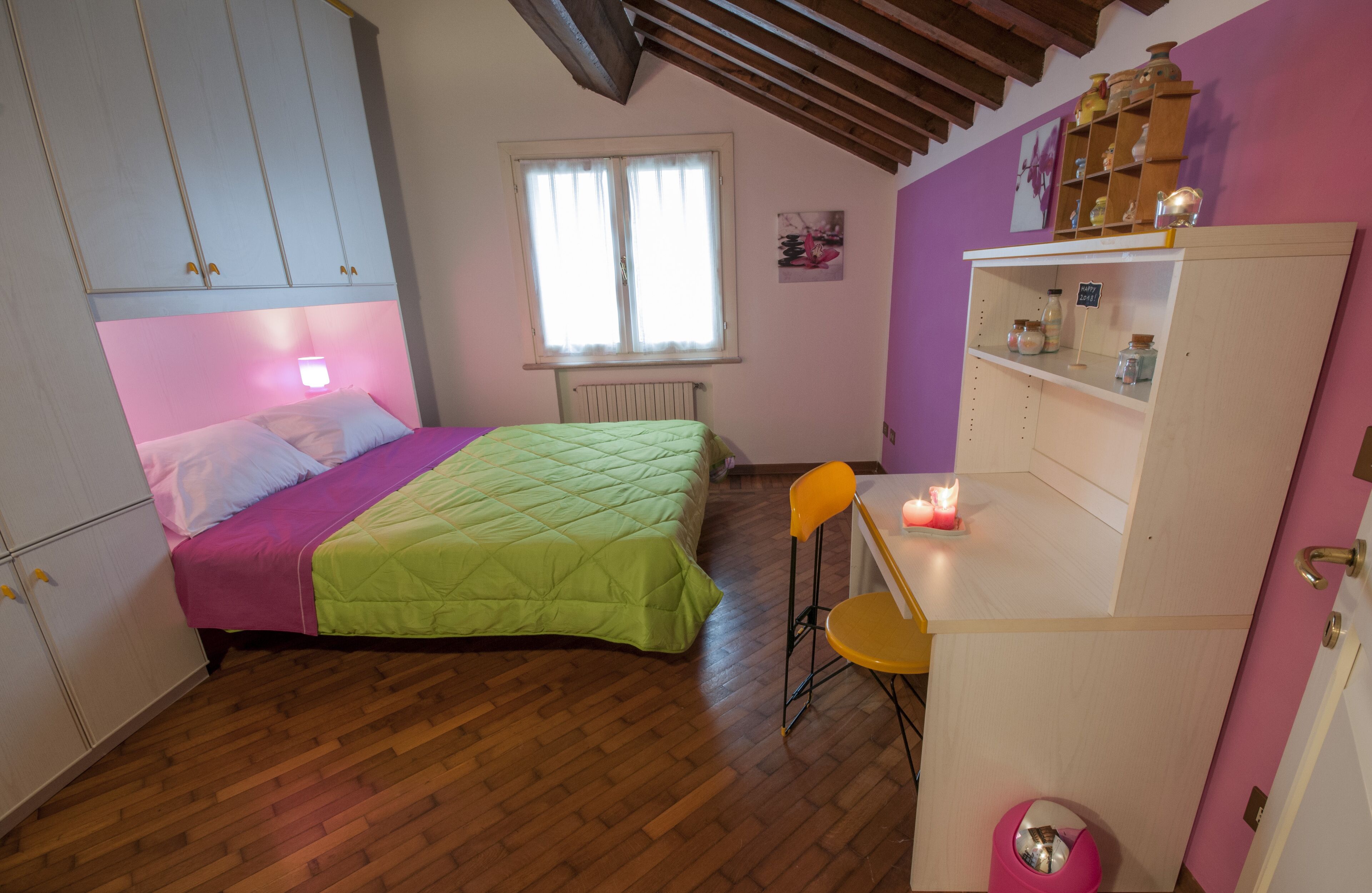 Quarto com cama, uma cadeira, escrivaninha e prateleira com potes.