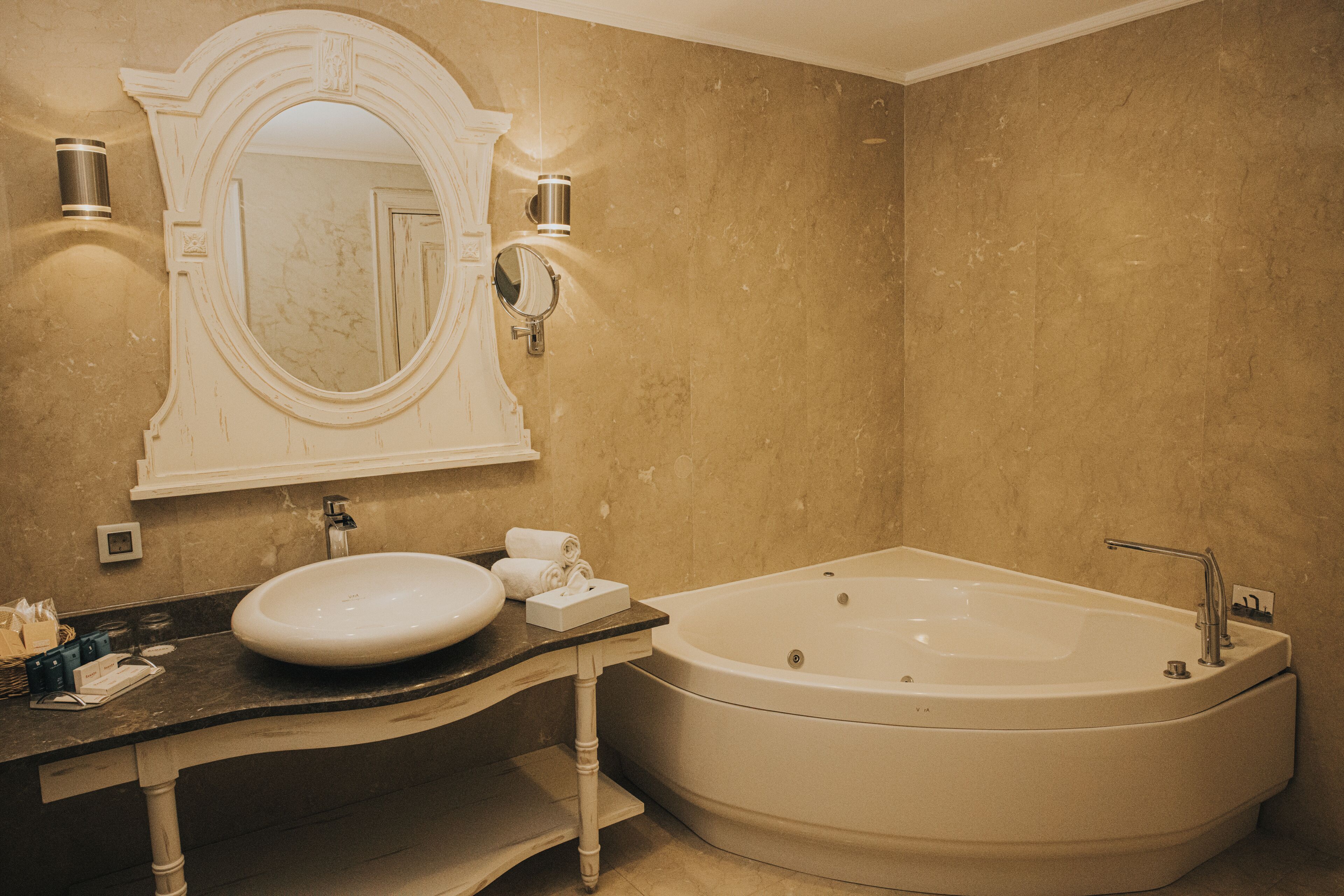 Um banheiro com uma banheira oval grande, pia redonda e espelho com moldura decorativa.