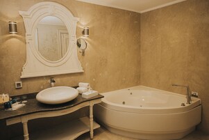 Um banheiro com uma banheira oval grande, pia redonda e espelho com moldura decorativa.