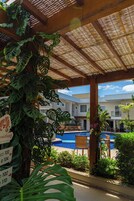Área externa coberta com piscina, pérgola de madeira e plantas tropicais.
