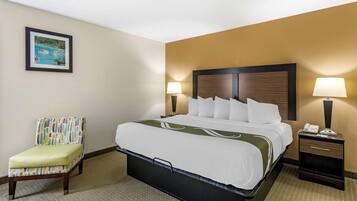 Quarto de hotel com cama, uma cadeira, mesa de cabeceira e luminária na parede.