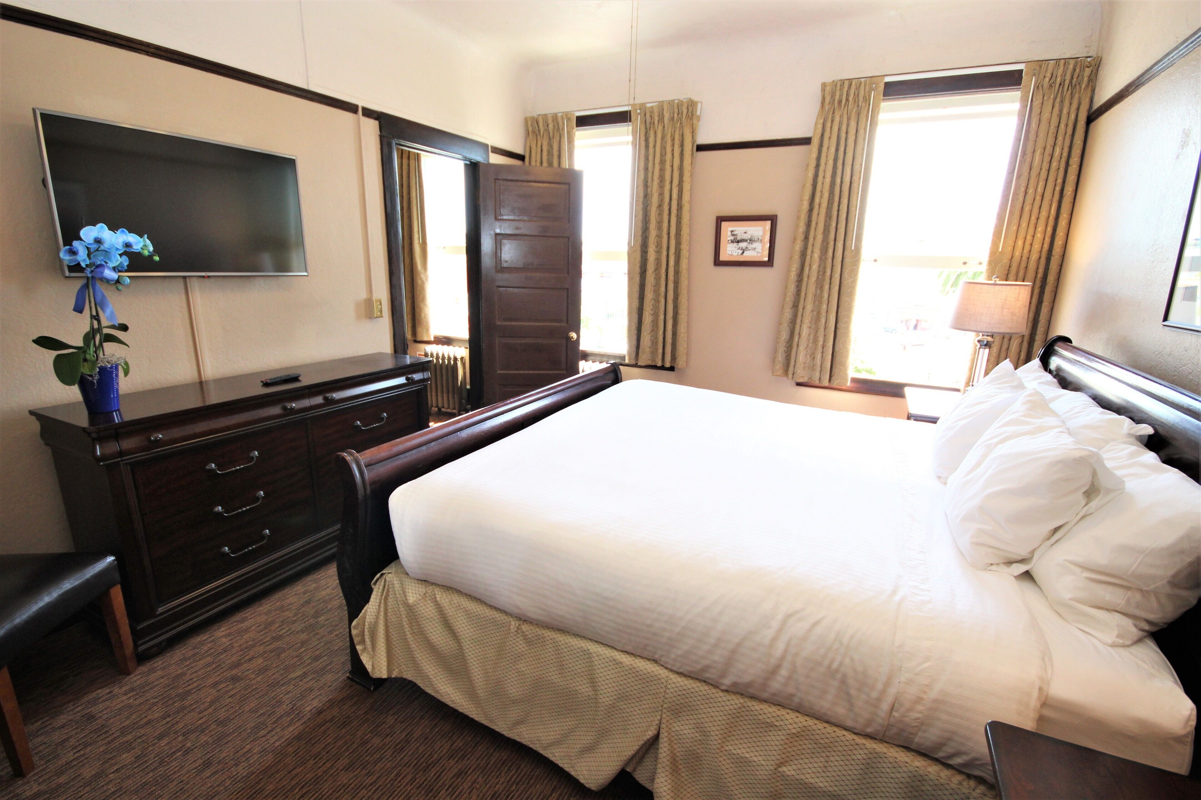 Quarto de hotel com cama grande, penteadeira, televisão na parede e janela com cortinas.