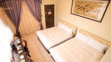 Quarto de hotel com duas camas, uma porta, um quadro emoldurado e uma mesa com chaleira e papéis.