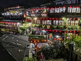 Um edifício tradicional de vários andares, com varandas, lanternas vermelhas e vegetação.
