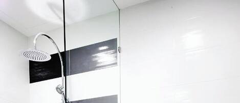 Casa de banho moderna com cabine de duche em vidro, sanita branca e um contentor de lixo.
