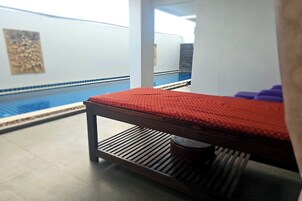 Área de piscina com um banco de madeira e uma pequena mesa, piso revestido e vista para a piscina.