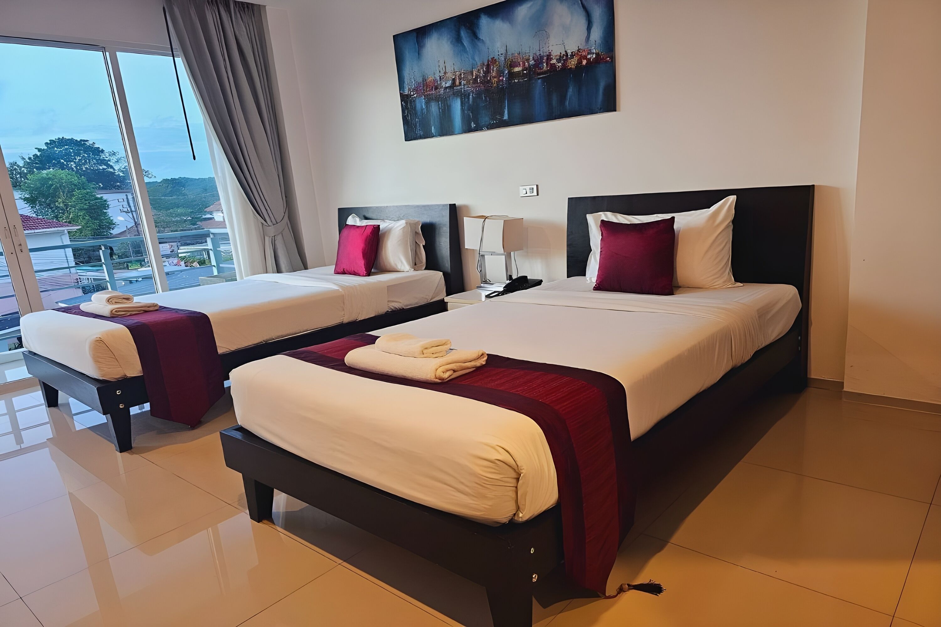 Quarto de hotel com duas camas, uma janela grande, um quadro e vista para o exterior.
