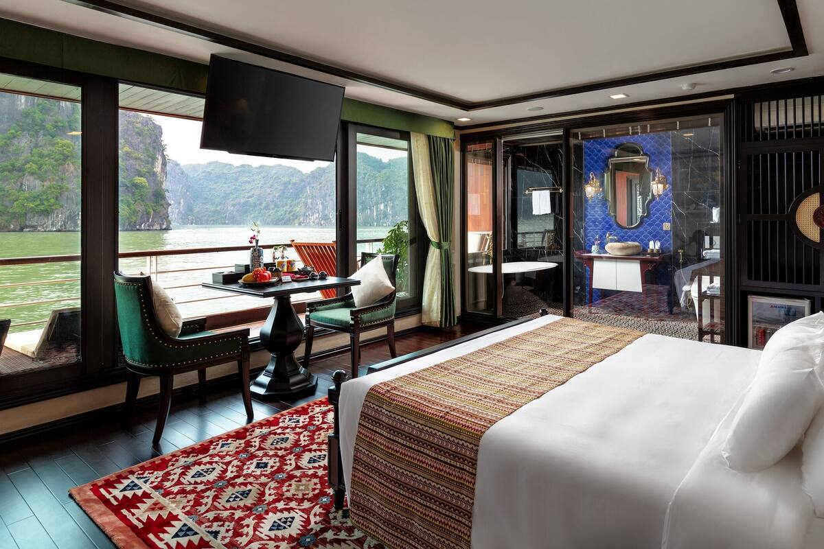 Quarto de hotel com uma cama grande, uma escrivaninha com cadeira, uma televisão e vista para a água.