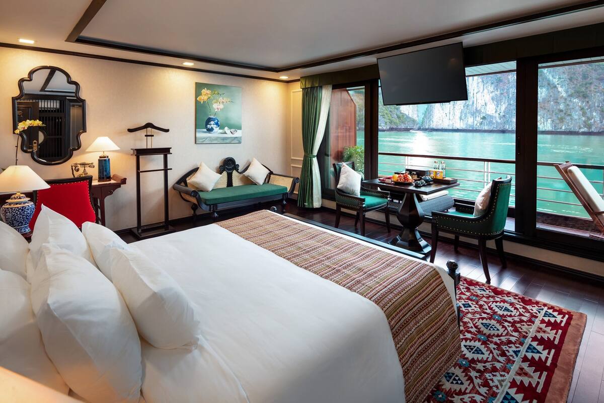 Quarto de hotel com uma cama grande, área de refeições, televisão e vista para um corpo de água.