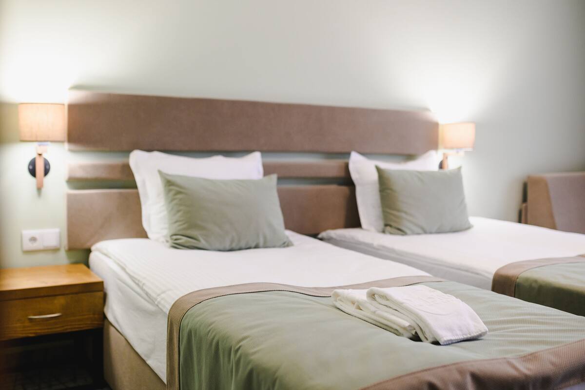 Quarto de hotel com duas camas, uma mesa de cabeceira e um abajur.
