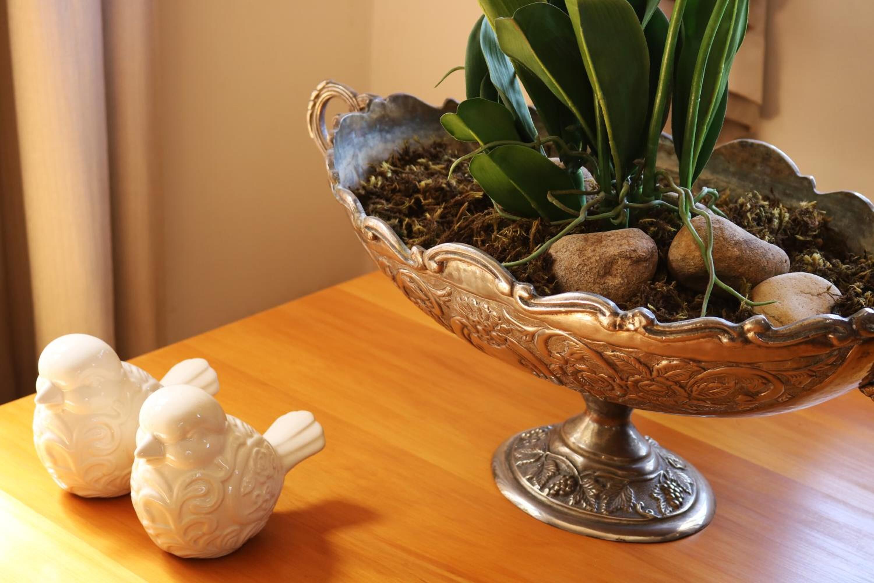 Uma taça de prata decorativa com uma planta e pedras sobre uma mesa de madeira.