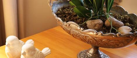 Uma taça de prata decorativa com uma planta e pedras sobre uma mesa de madeira.