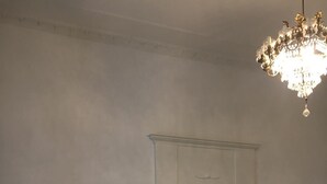 Uma sala de estar com sofá, poltrona, mesa de centro e lustre. Há duas molduras com quadros na parede.