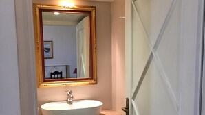 Casa de banho com uma pia branca, um espelho com moldura dourada e uma porta branca com padrão de losangos.