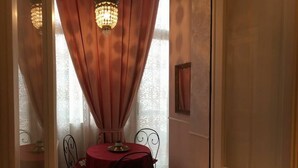 Uma sala de jantar com uma mesa redonda, duas cadeiras, um candelabro e uma janela com cortinas.