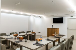 Uma sala de conferência com uma mesa comprida, cadeiras, um púlpito e uma TV de tela plana na parede.