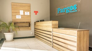 Balcão de recepção com acabamento em madeira, uma planta em vaso e uma placa com a inscrição 'Pargos Pousada'.