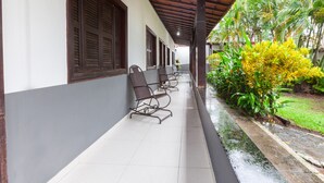 Uma área externa coberta com piso de azulejos, persianas de madeira e cadeiras de metal.