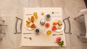 Mesa de café da manhã posta com diversos alimentos, incluindo pão, ovos e salada de frutas, além de xícaras de café e suco.