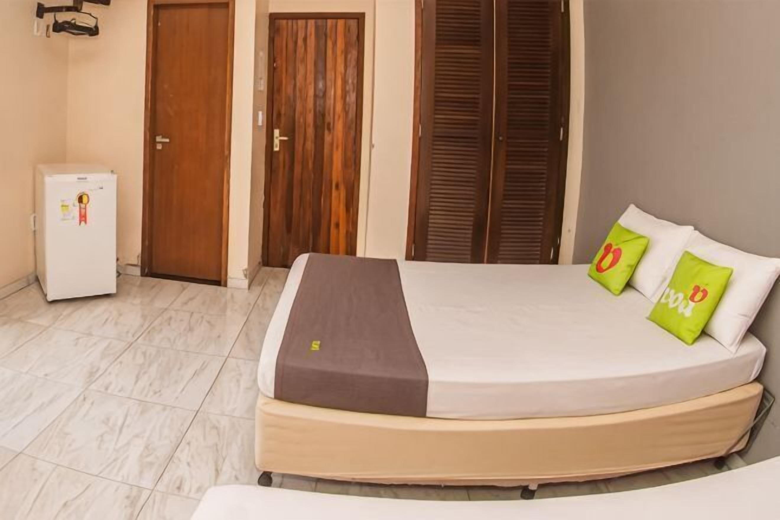 Quarto com uma cama, um pequeno frigorífico e portas de madeira.