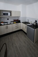 Uma cozinha moderna com armários de madeira clara, lava-louças de aço inoxidável, micro-ondas e uma pia com chaleira.
