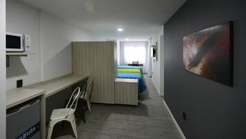 Quarto de hotel com cama, escrivaninha com cadeira, micro-ondas e um quadro na parede.