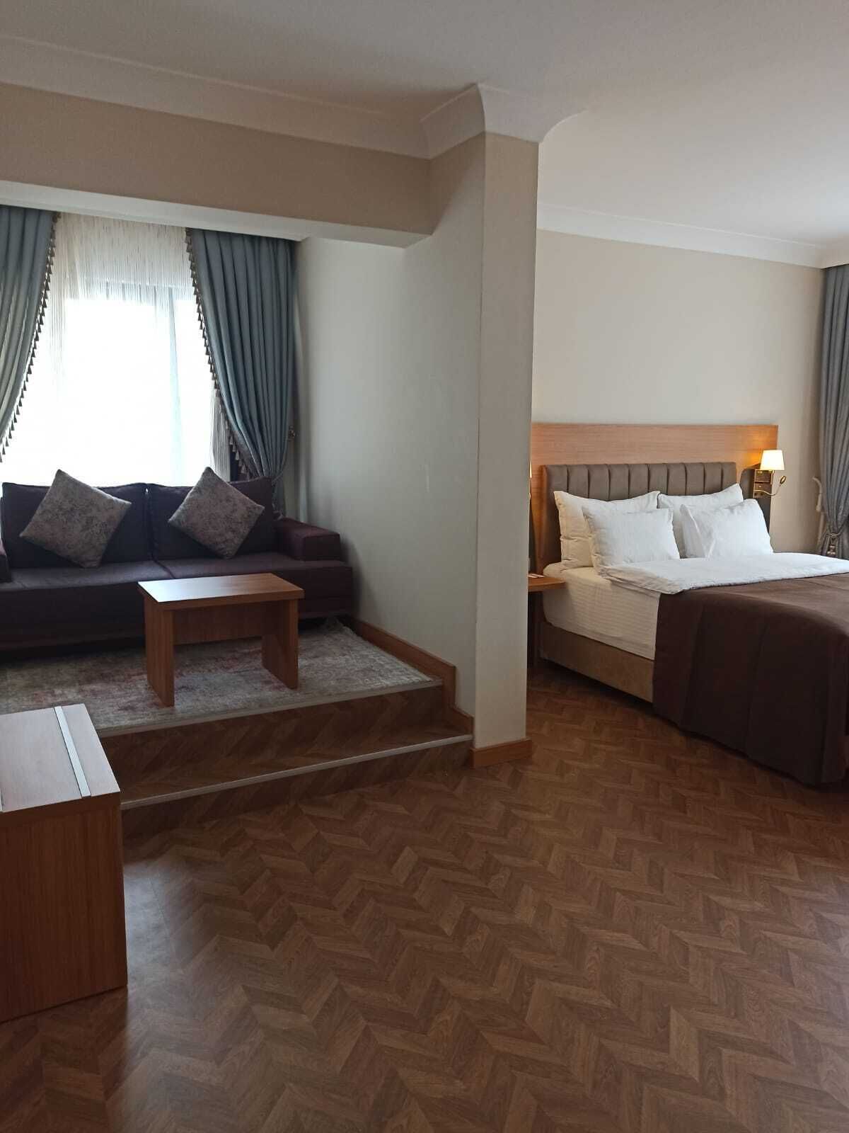 Quarto de hotel com cama, sofá, mesa de centro e criado-mudo.