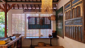 Quarto tradicional com teto de madeira, luminária pendente de fibras naturais, janela com padrão de treliça e parede com painéis decorativos.