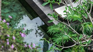 Uma área à beira da piscina com espreguiçadeiras e guarda-sóis, um deck de madeira e um pequeno jardim.