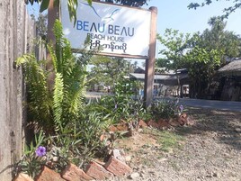 Placa para "BEAU BEAU BEACH HOUSE", com uma cerca de madeira e plantas em primeiro plano.