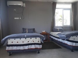 Quarto de hotel com duas camas, uma mesinha, ar condicionado e janela com cortinas.