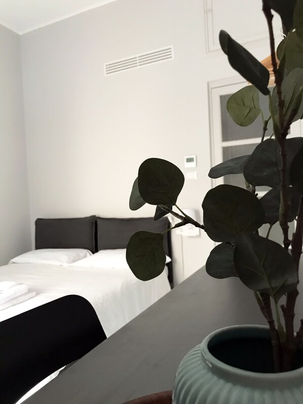 Quarto de hotel com uma cama, mesa de cabeceira e planta em vaso.
